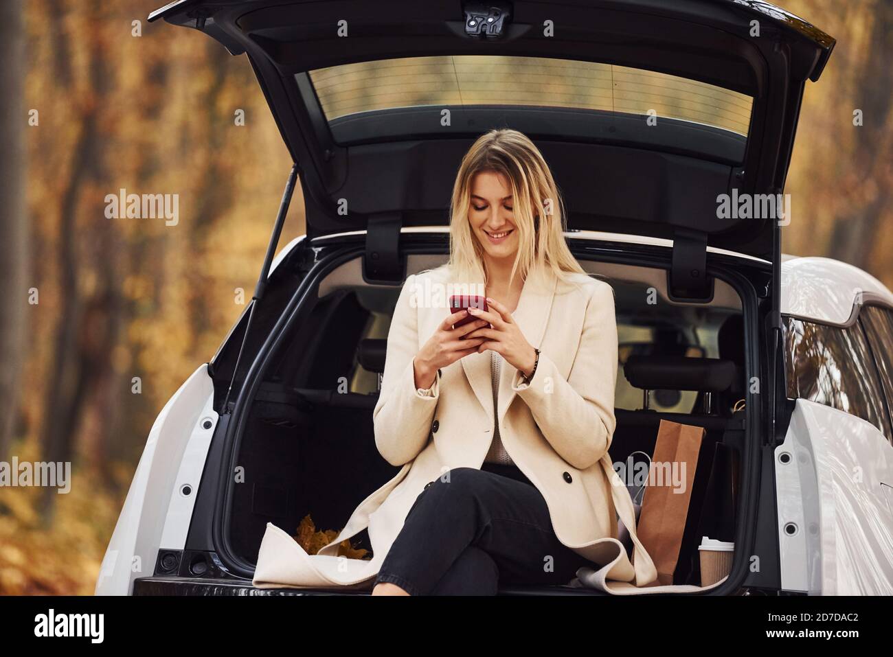 Girl sits on the back of car. Modern brand new automobile in the forest ...