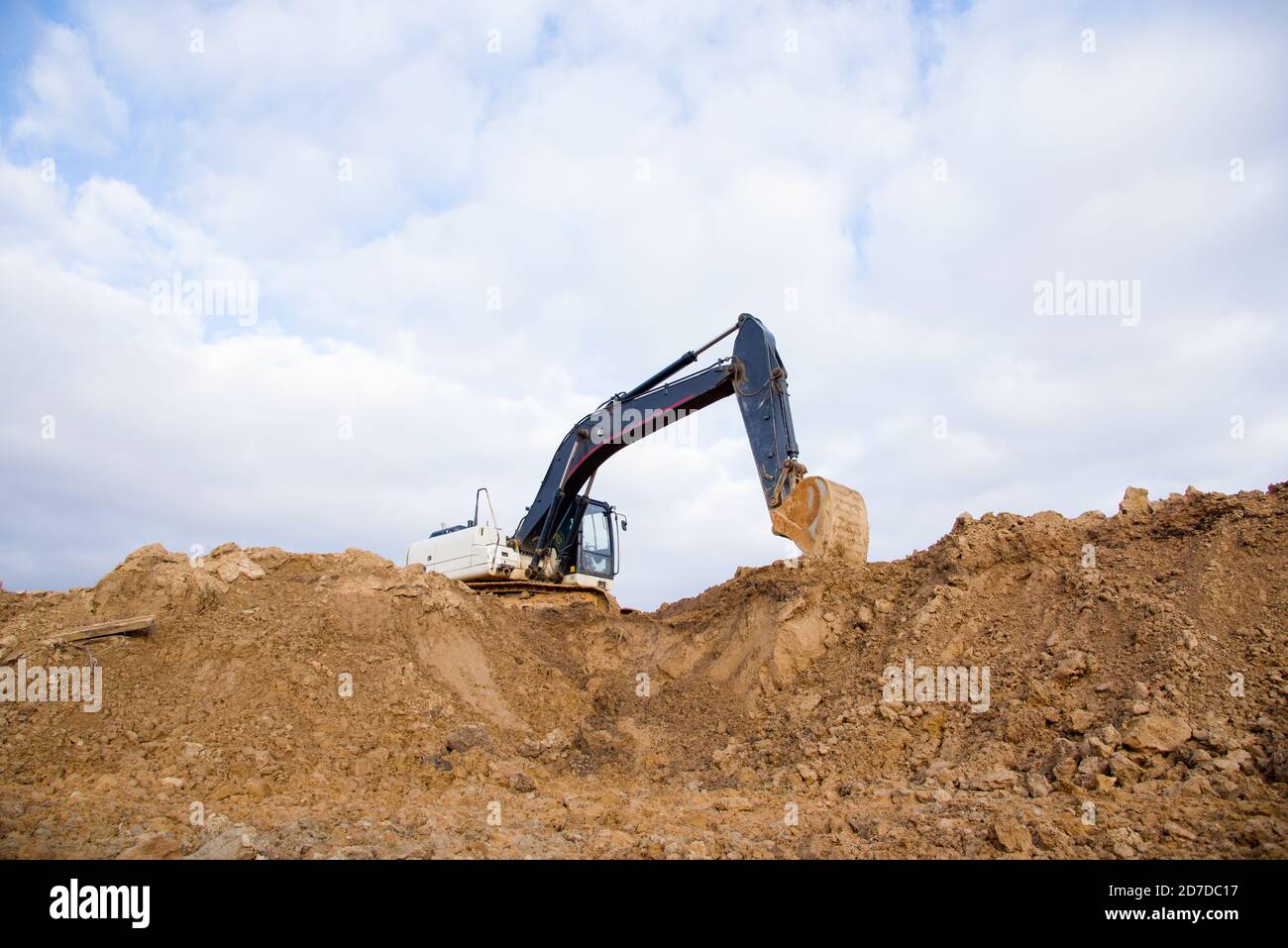 Black and white excavator during earthworks at construction site ...