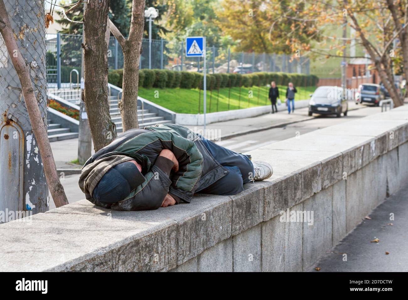 Poor homeless man or refugee sleeping on the street in the city ...