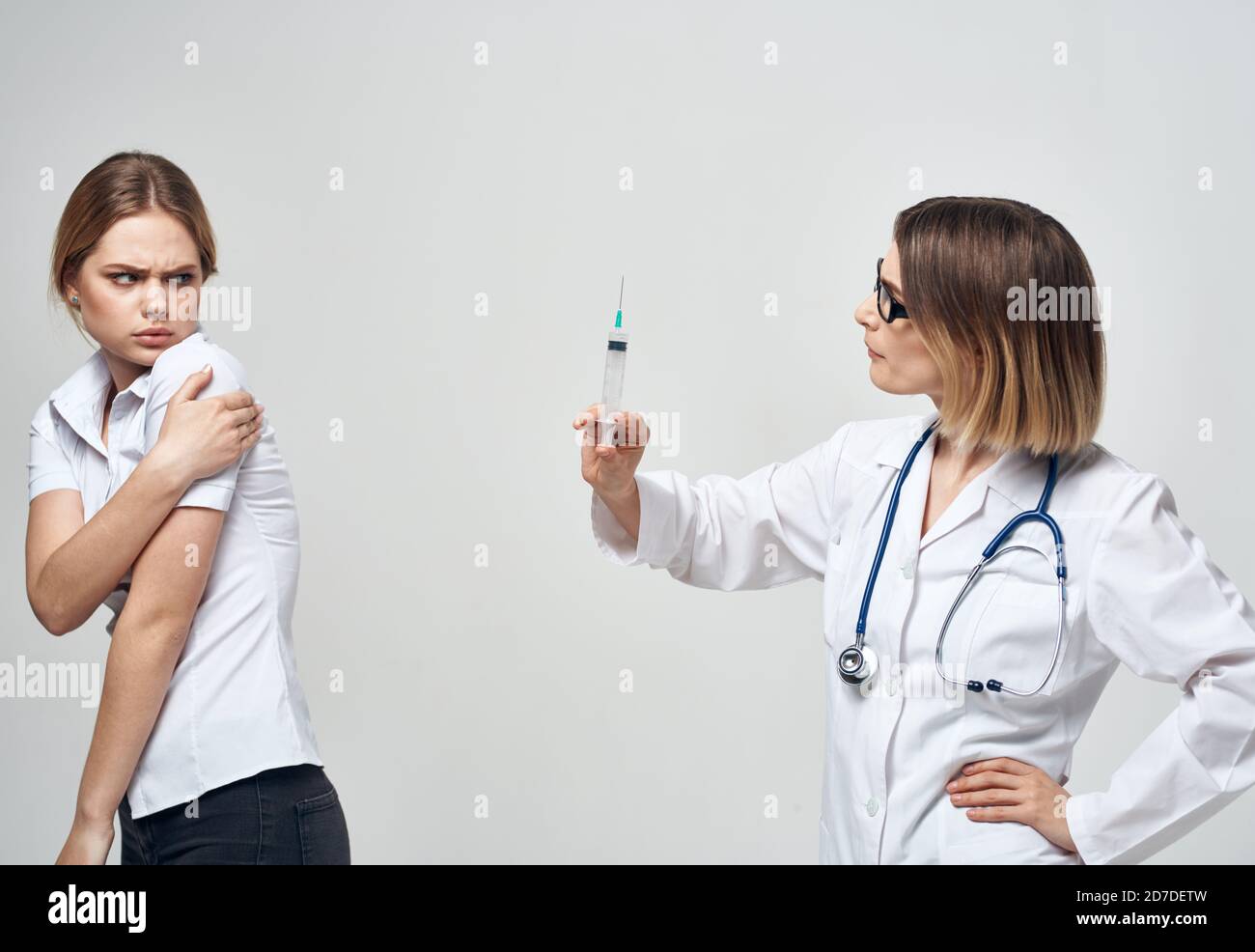 Frightened patient and nurse with a syringe in hand on a light ...