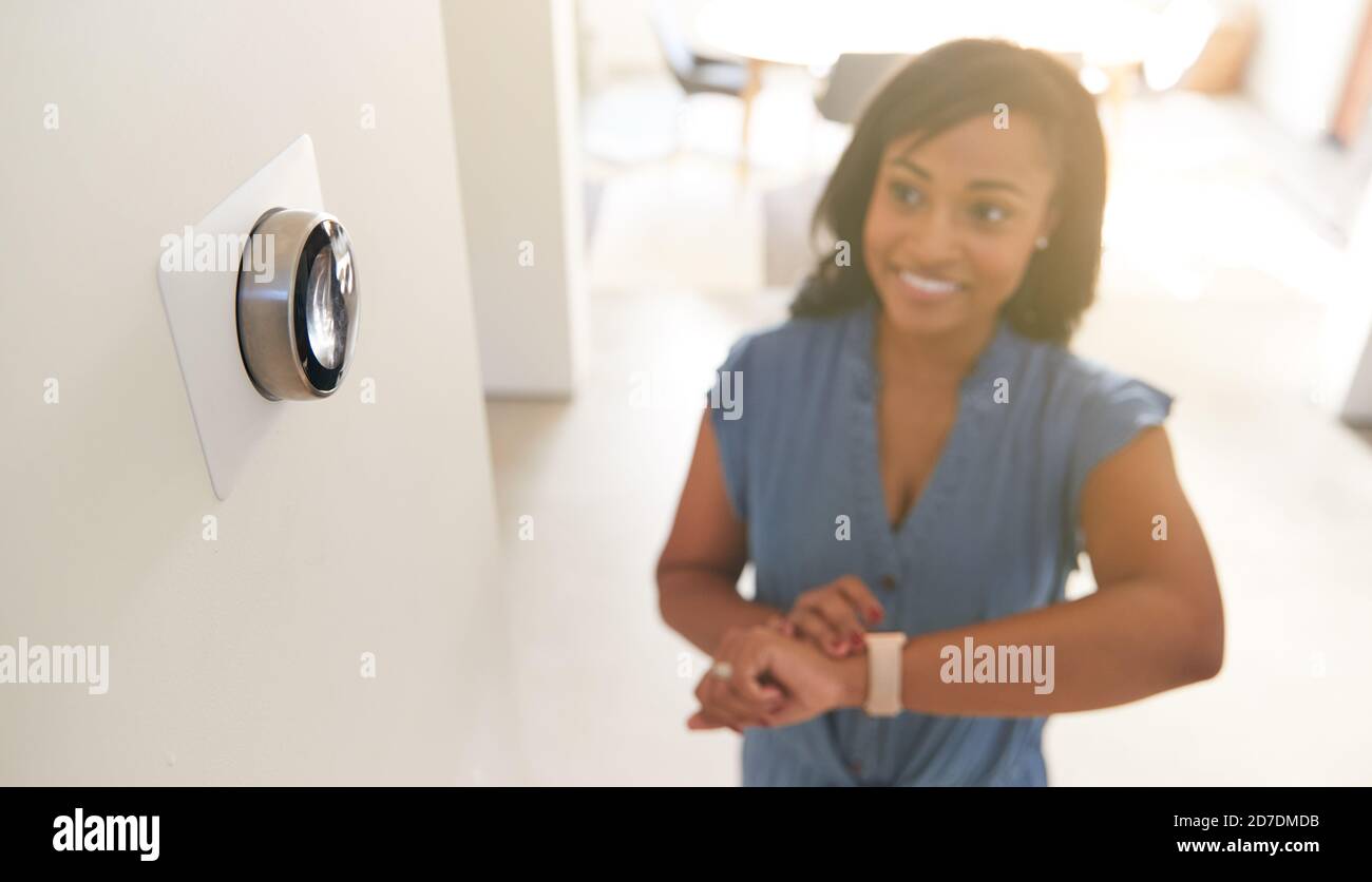 Woman Adjusting Digital Central Heating Thermostat Using Smart Watch At ...