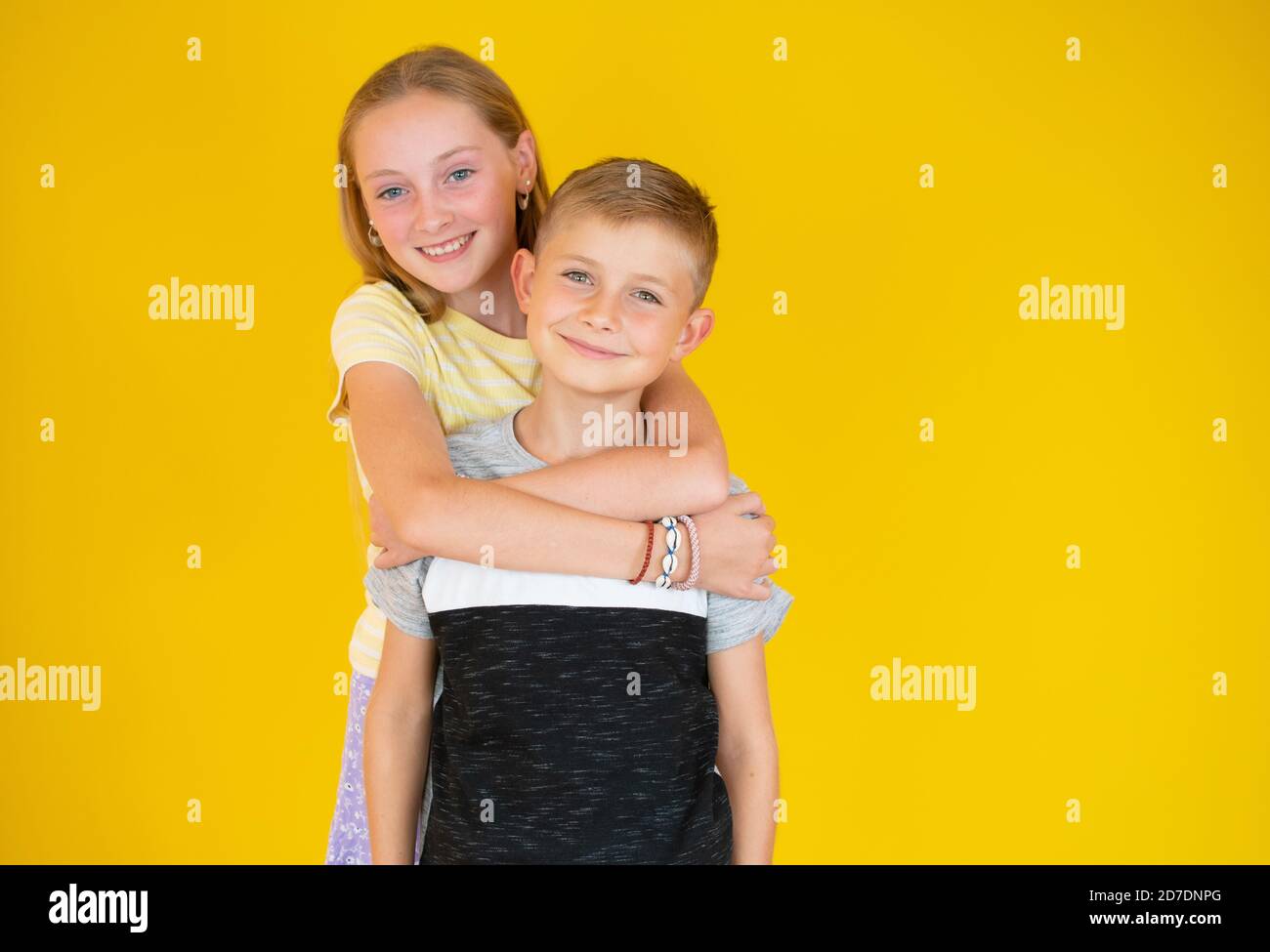 Happy brother and sister hugging each other over yellow background ...