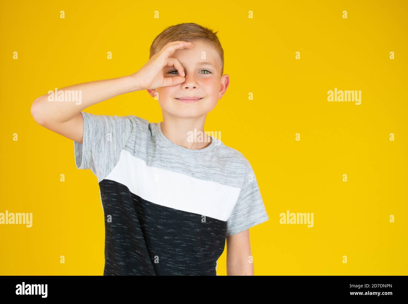 Portrait of handsome boy making okay Gesture with hand on eyes looking ...