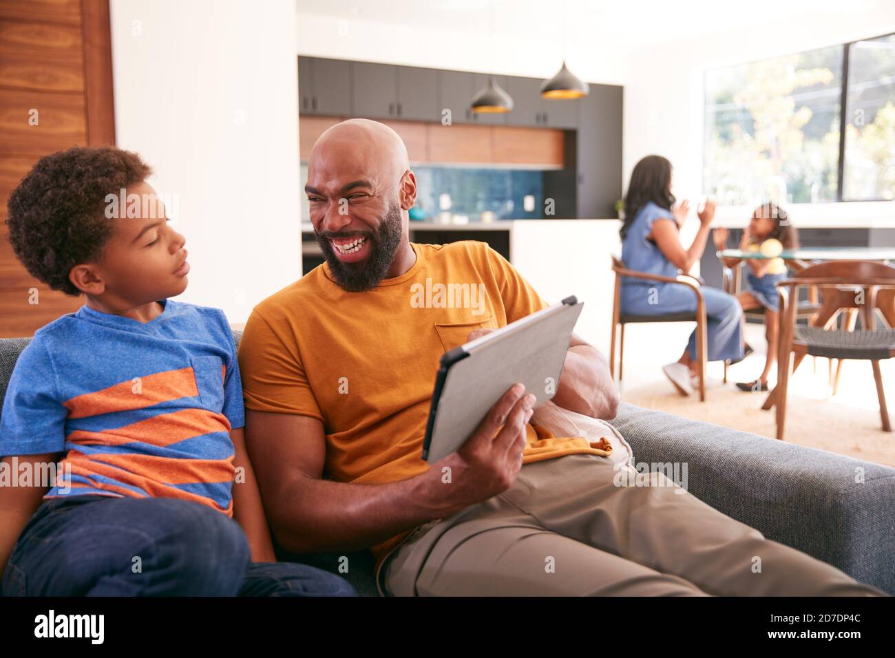 African American Father And Son Sitting On Sofa At Home Using Digital ...