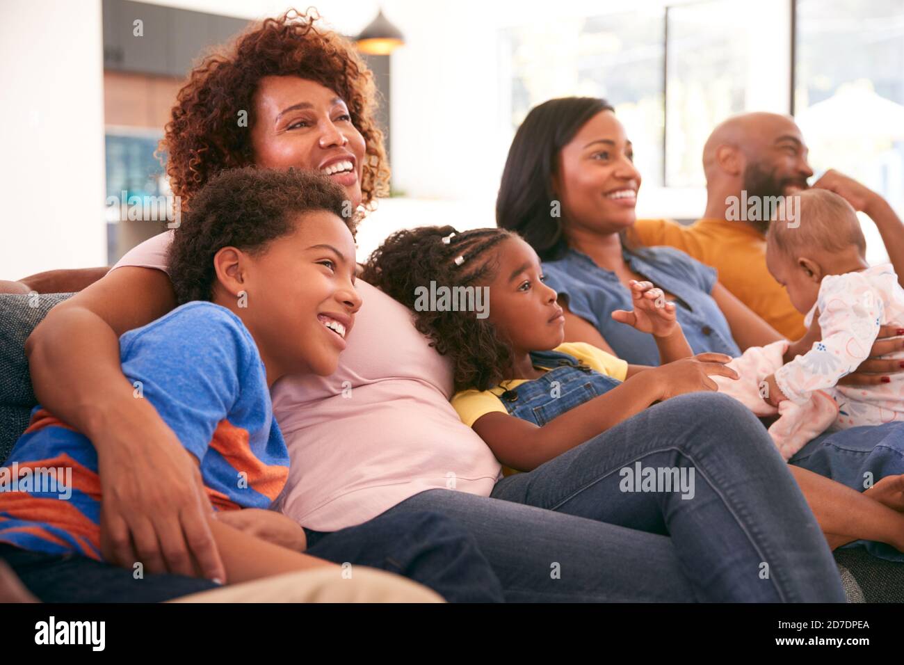 Multi-Generation African American Family Relaxing At Home Sitting On Sofa Watching TV Together ...
