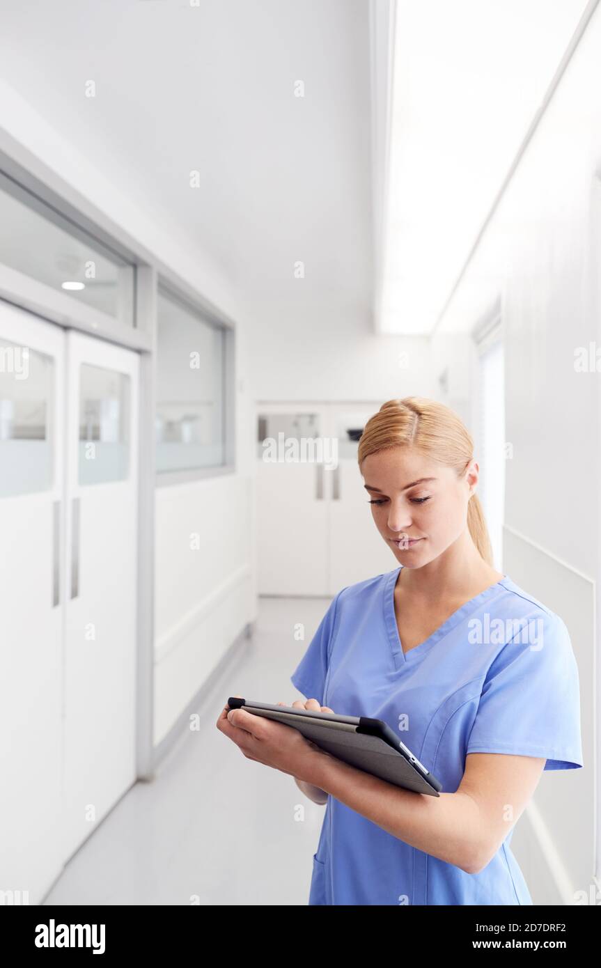 Female Doctor Wearing Scrubs In Hospital Corridor Using Digital Tablet ...