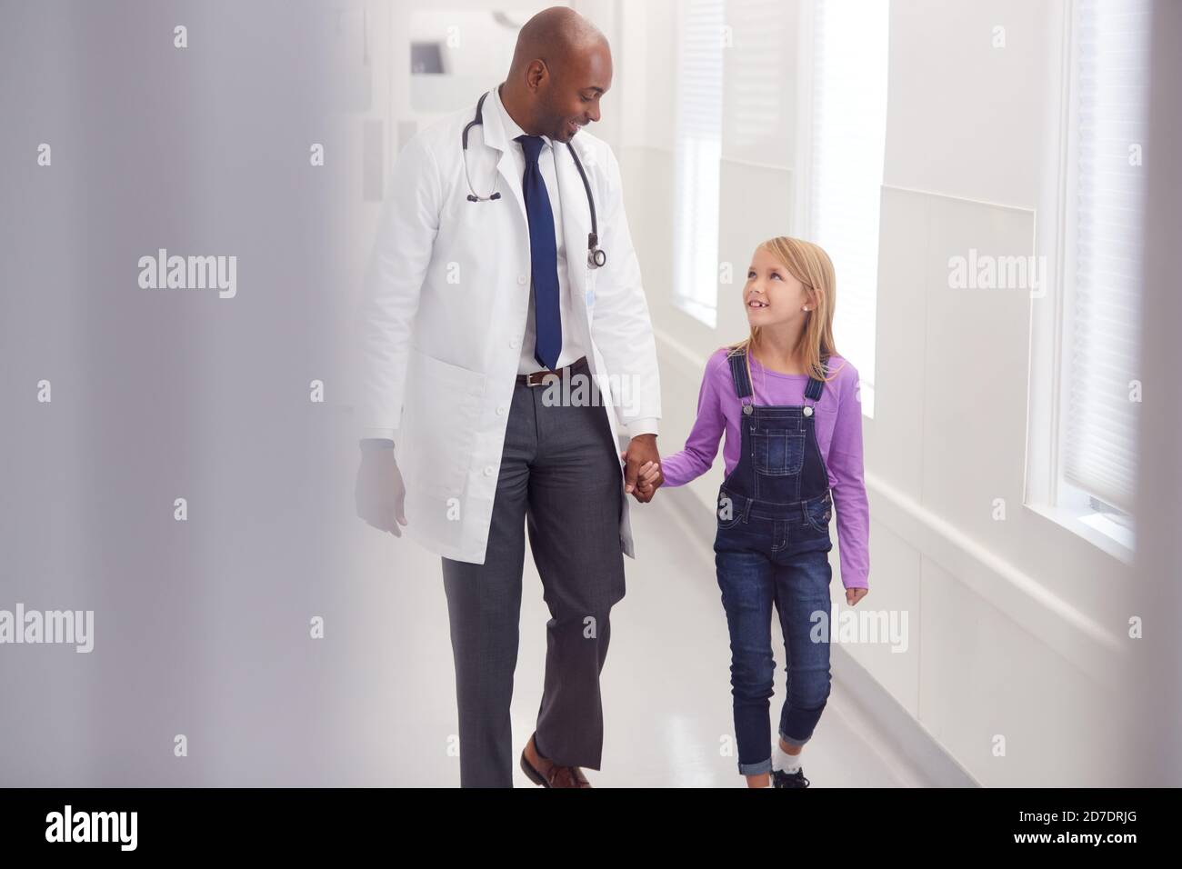 Male Paediatric Doctor Walking Along Hospital Corridor Holding Hands ...