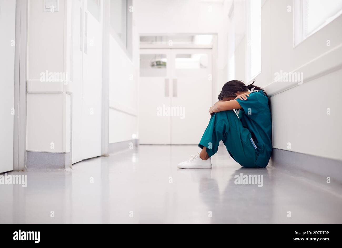 Stressed And Overworked Female Doctor Wearing Scrubs Sitting On Floor ...
