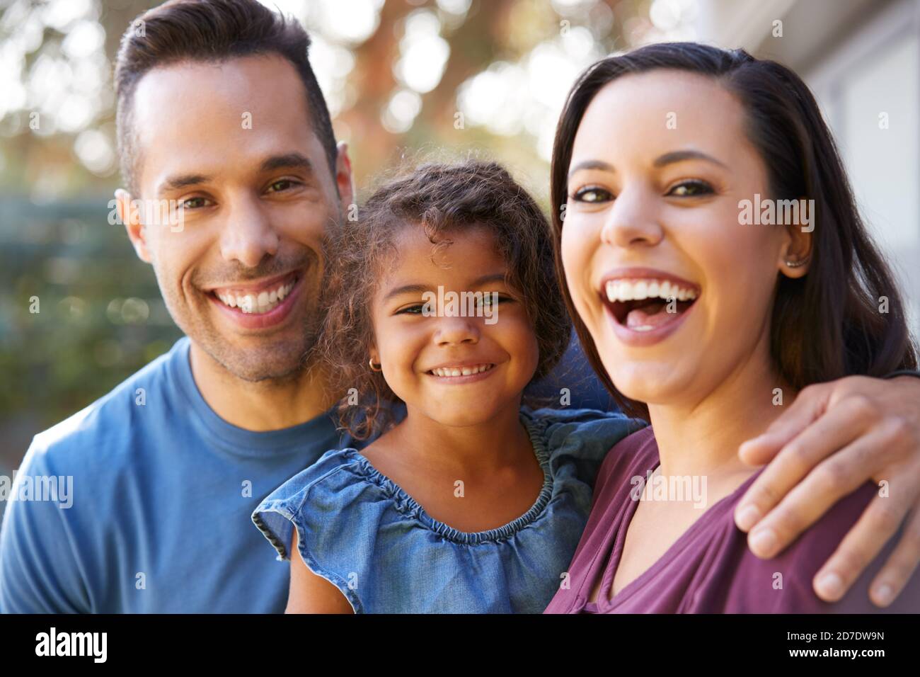 Portrait Of Smiling Hispanic Family With Daughter Laughing In Garden At ...