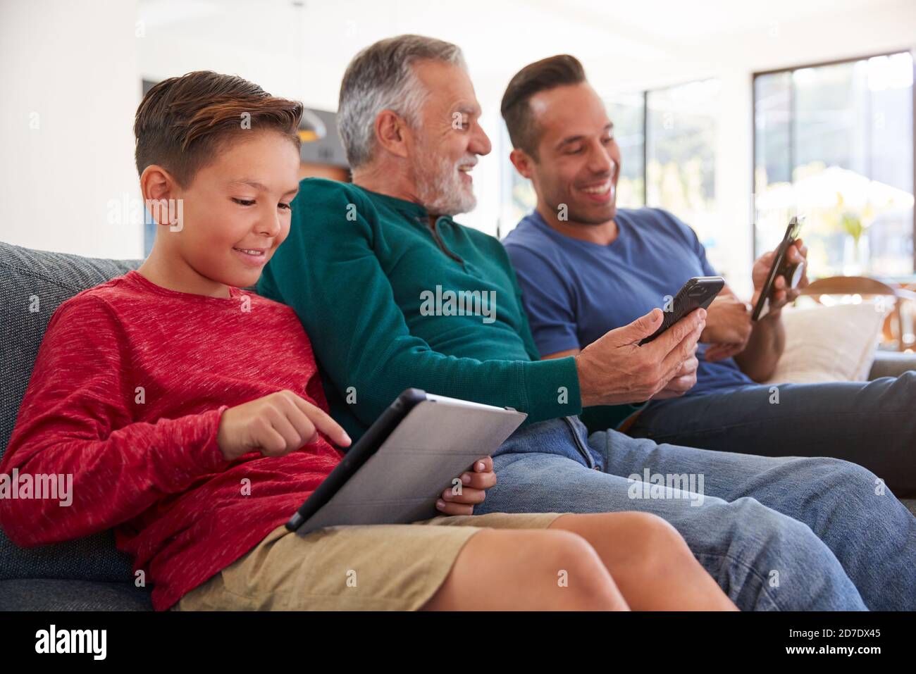 Multi-Generation Male Hispanic Family Sitting On Sofa At Home Using ...