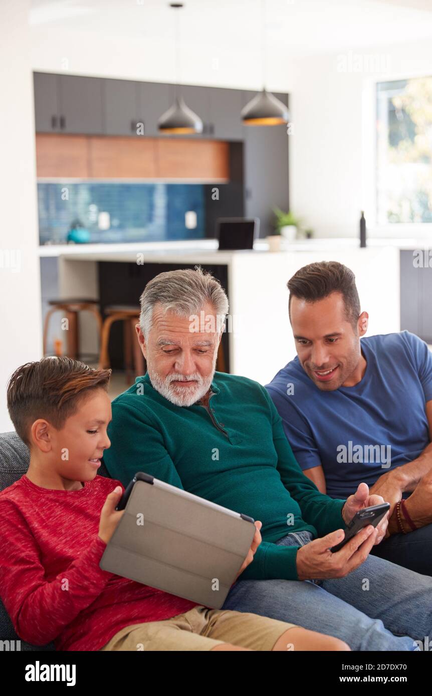 Multi-Generation Male Hispanic Family Sitting On Sofa At Home Using ...