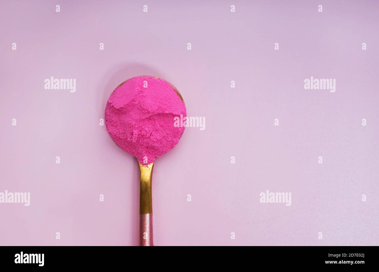Pink dragonfruit or other superfood powder in a spoon on pink ...