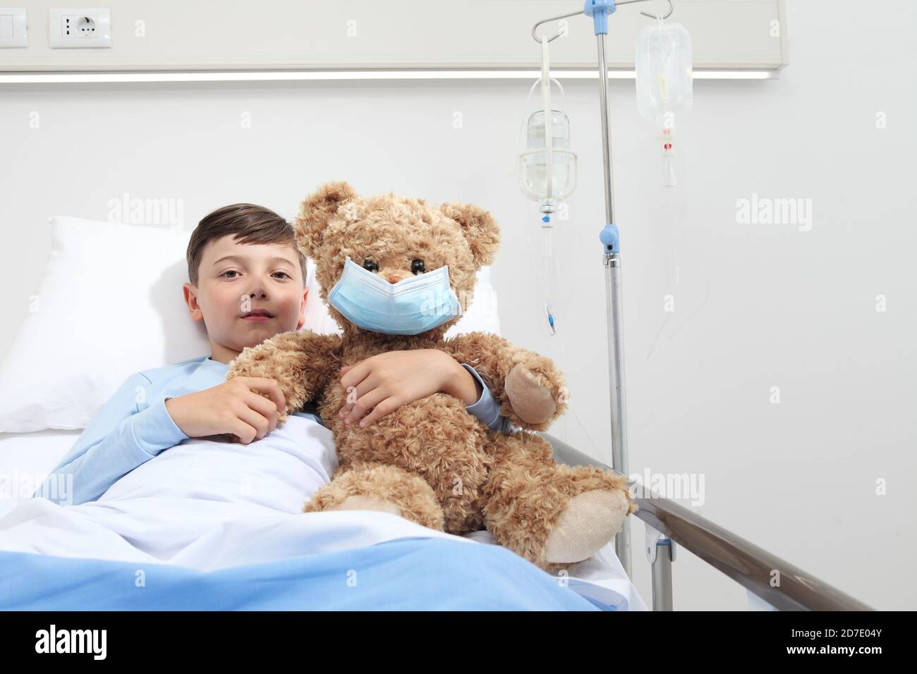 child in hospital bed with teddy bear wearing protective mask, corona ...
