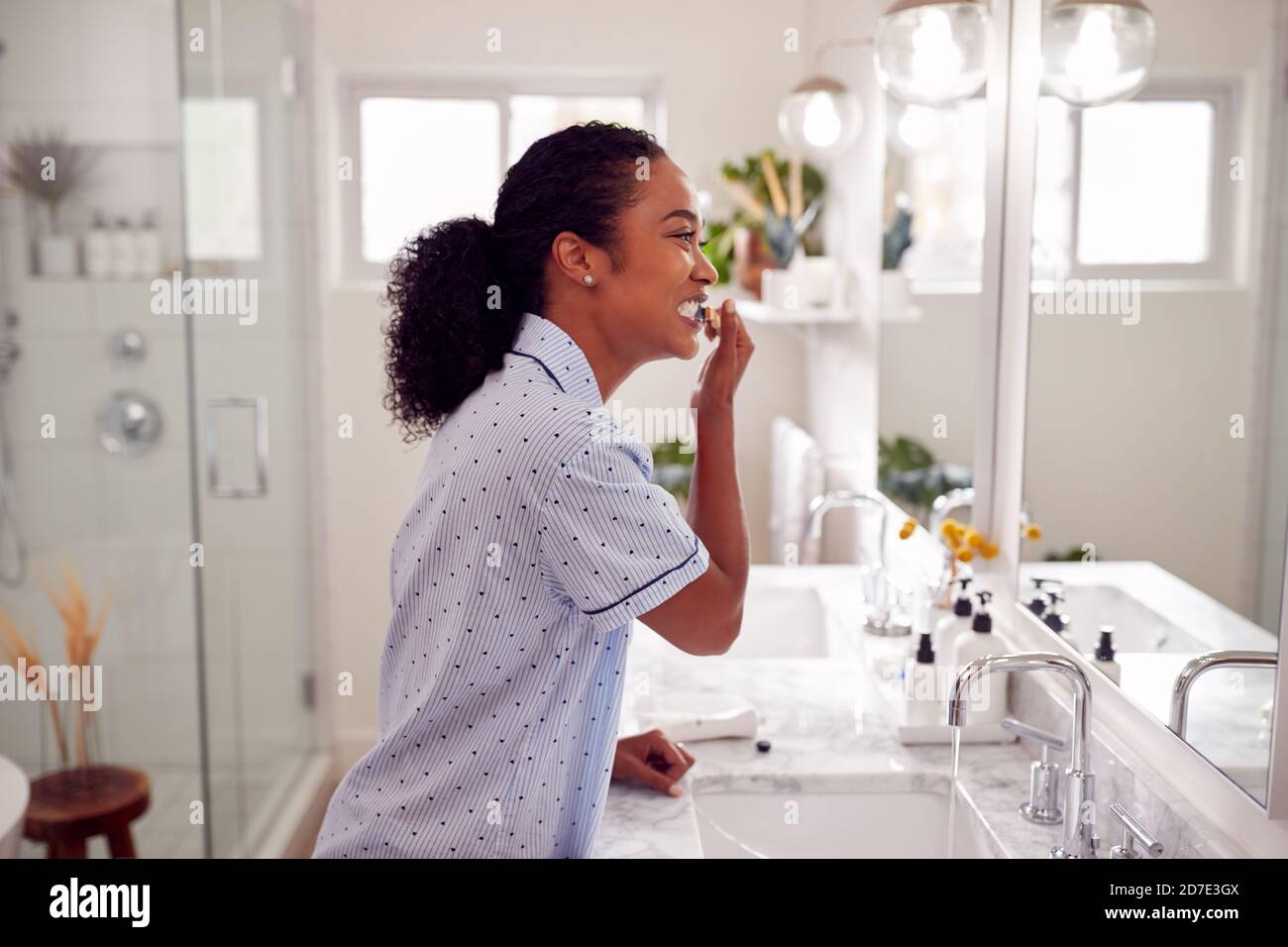 Woman Wearing Pyjamas Standing At Sink Brushing Teeth In Bathroom Stock ...