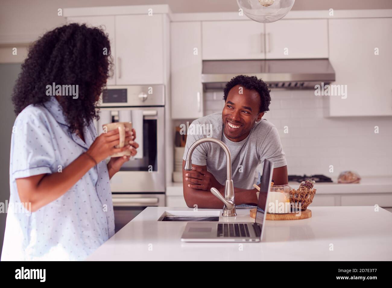 Couple Wearing Pyjamas Standing In Kitchen Working From Home On Laptop ...