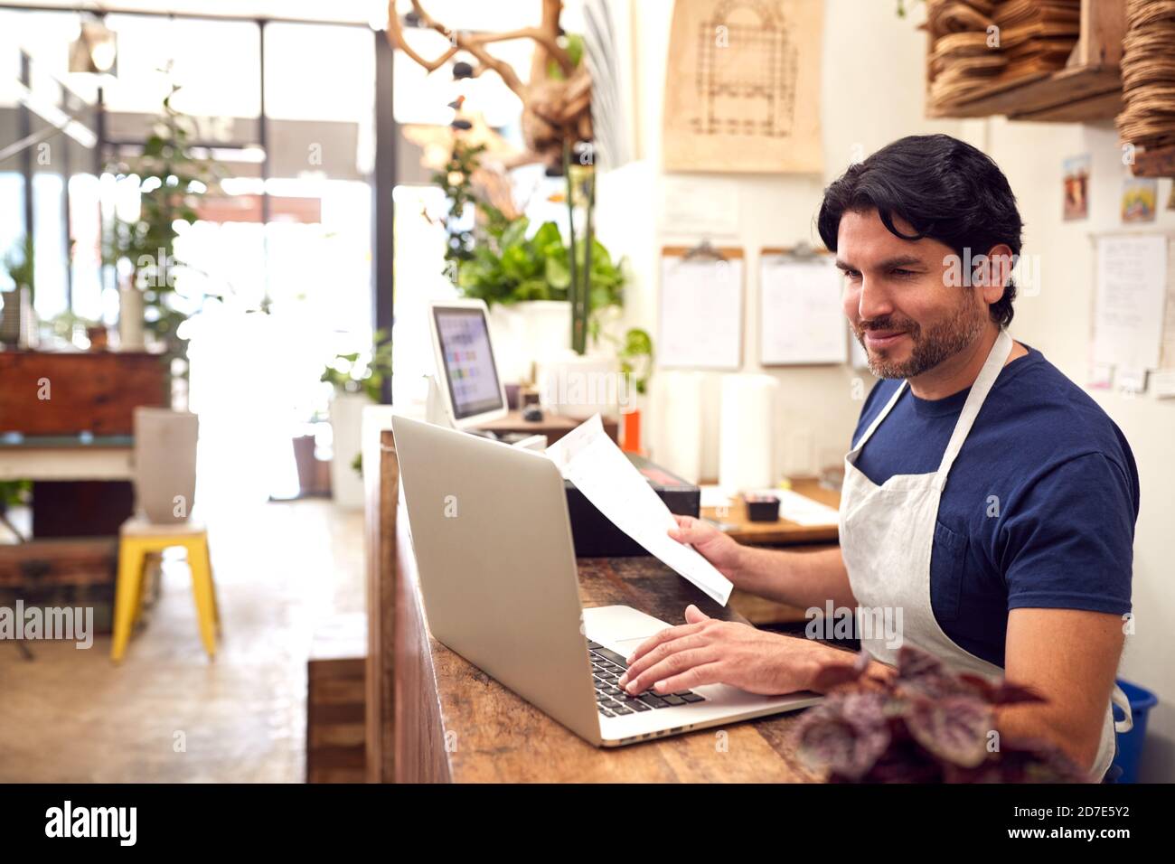 Male Sales Assistant Working On Laptop Behind Sales Desk Of Florists ...