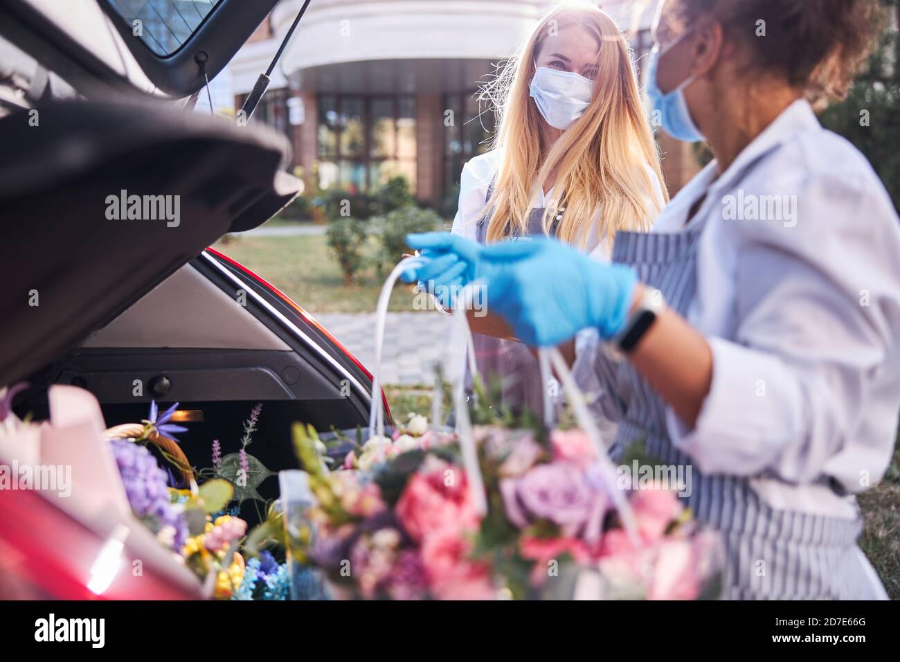 Professional flower shop workers packing bags with flowers into car ...