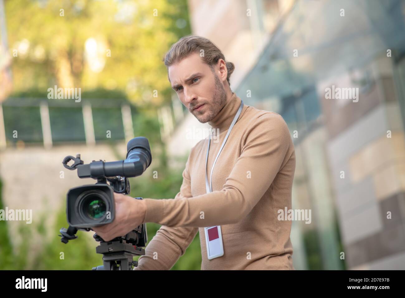 Concentrated cameraman standing behind camera, getting ready for ...