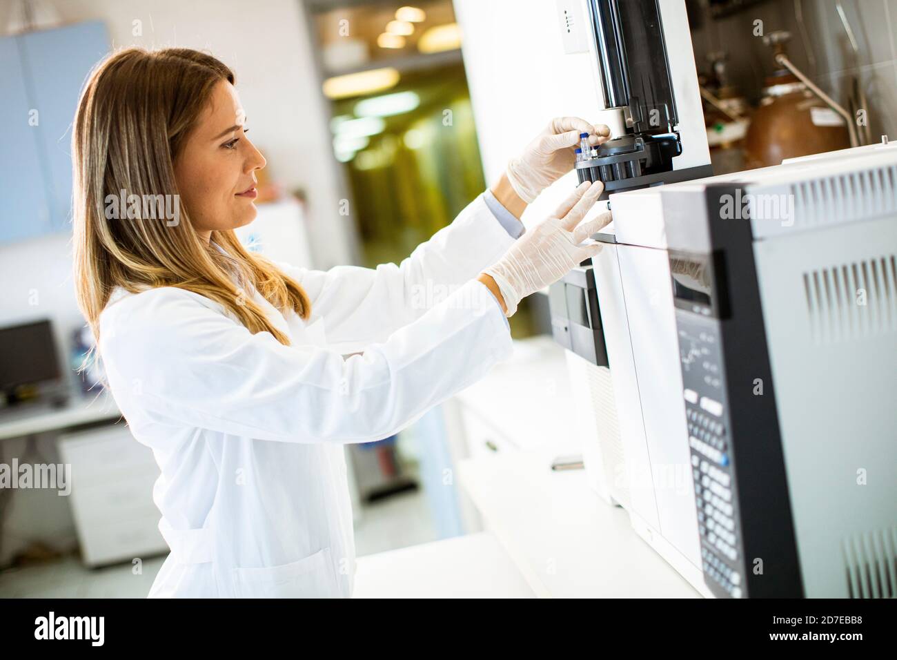 Young female scientist in a white lab coat putting vial with a sample ...