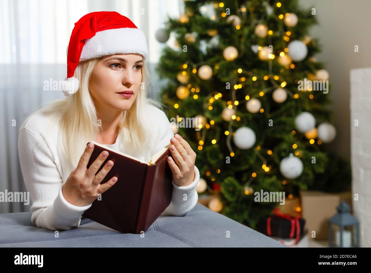 Beautiful young woman praying in front of the decorated Christmas tree ...