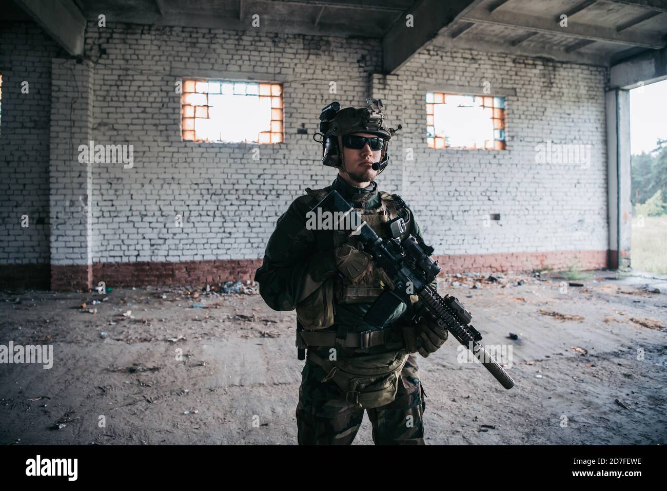 Military man with assault rifle standing inside building, he is ready ...