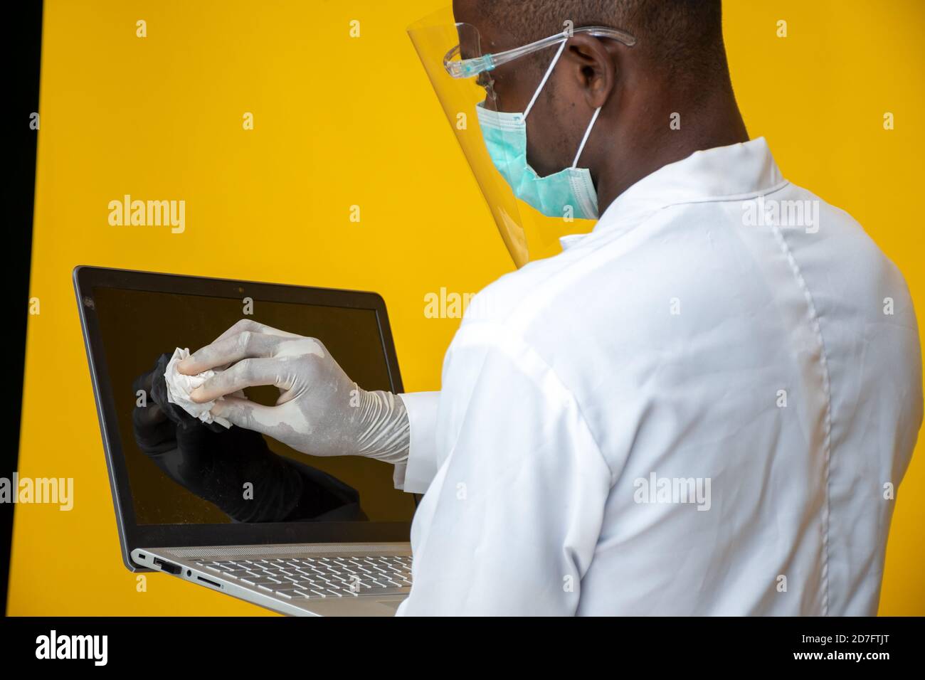 a young black man wearing a lab coat and face mask and shield cleaning ...
