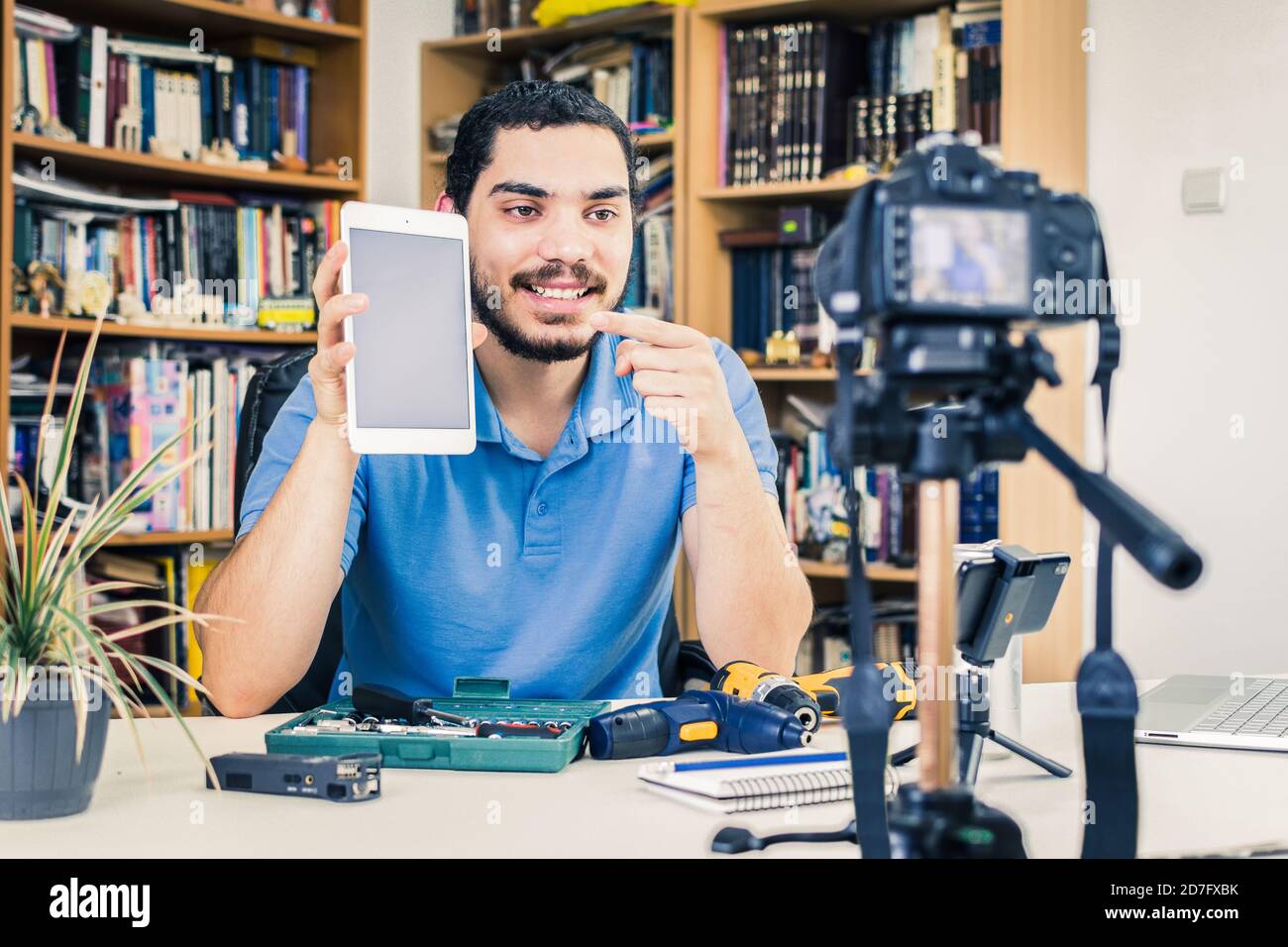 Young cheerful vlogger man filming his brand new tablet in his office ...