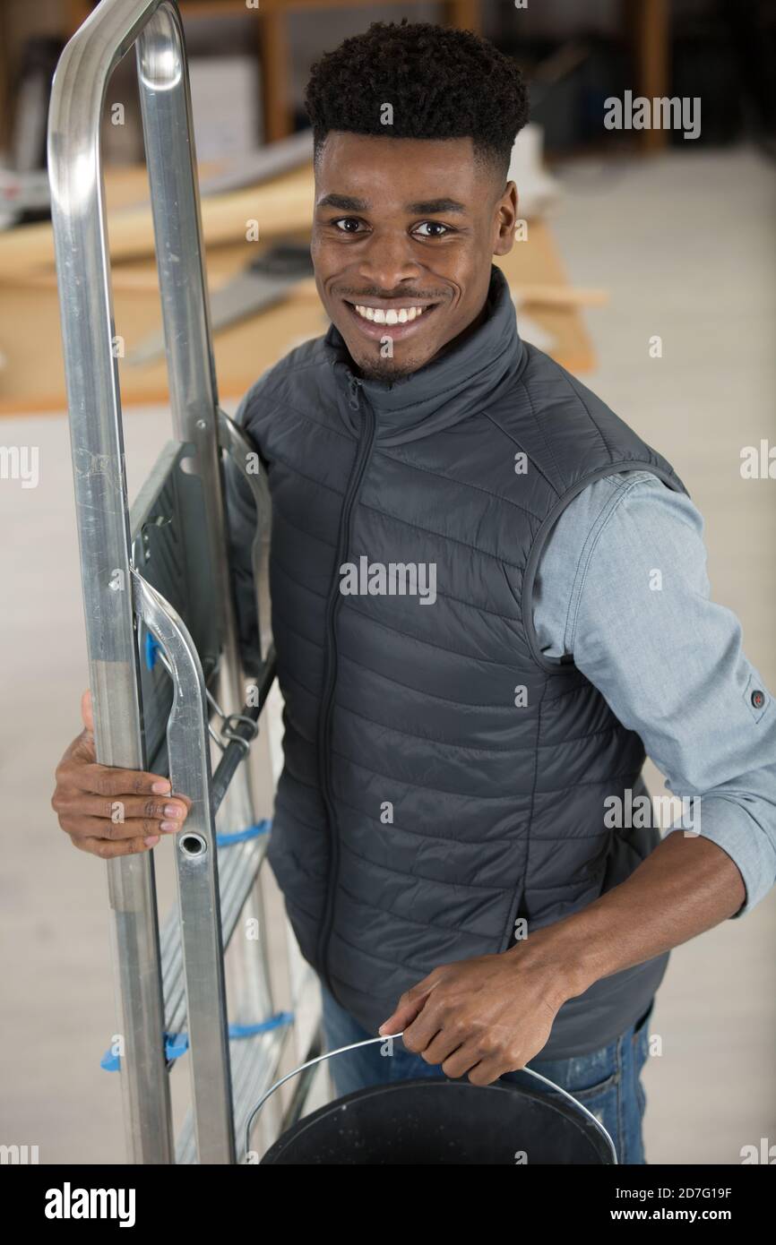 workman on site carrying a stepladder and bucket Stock Photo - Alamy