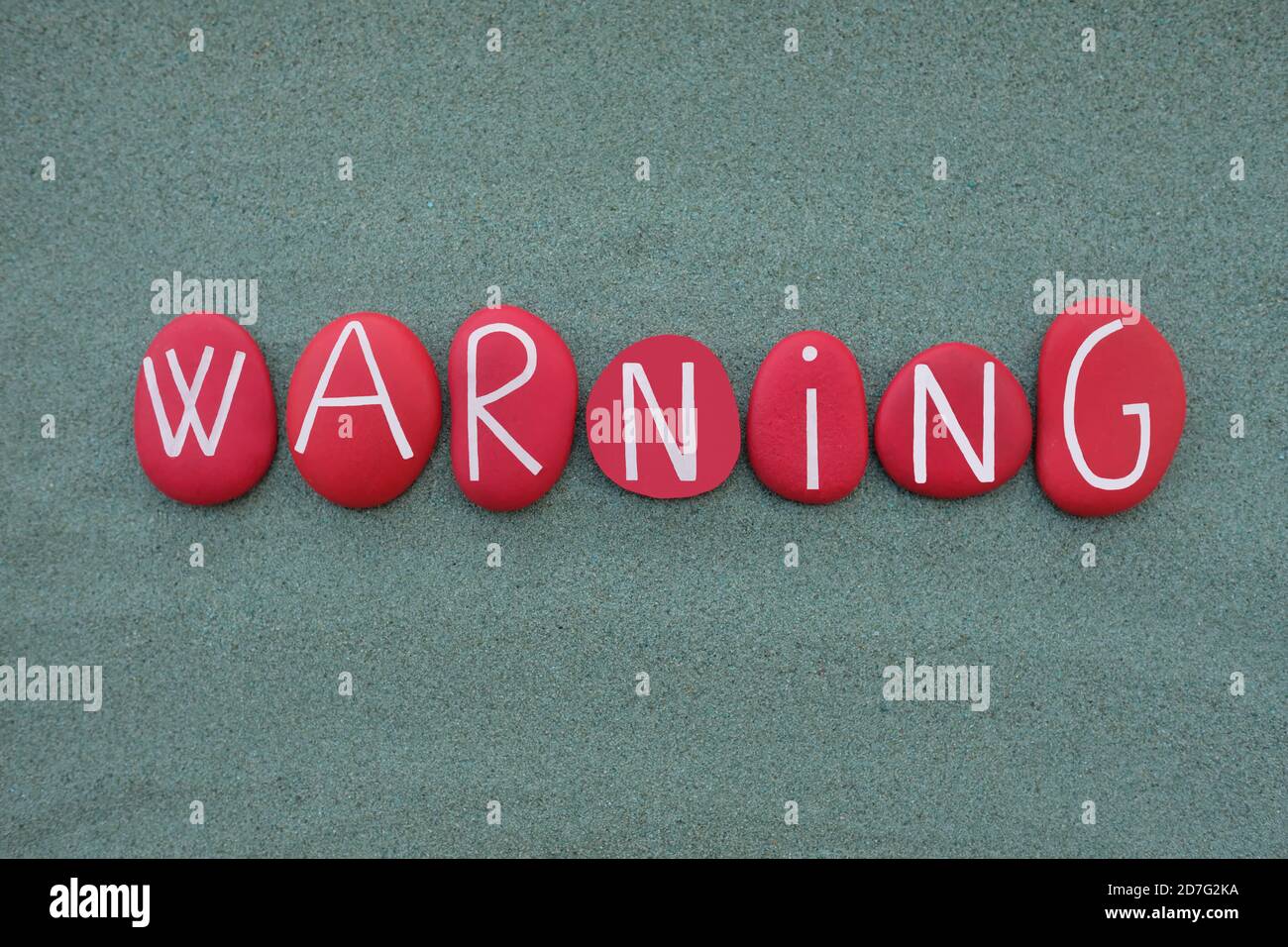 Warning text composed with red colored stone letters over green sand ...