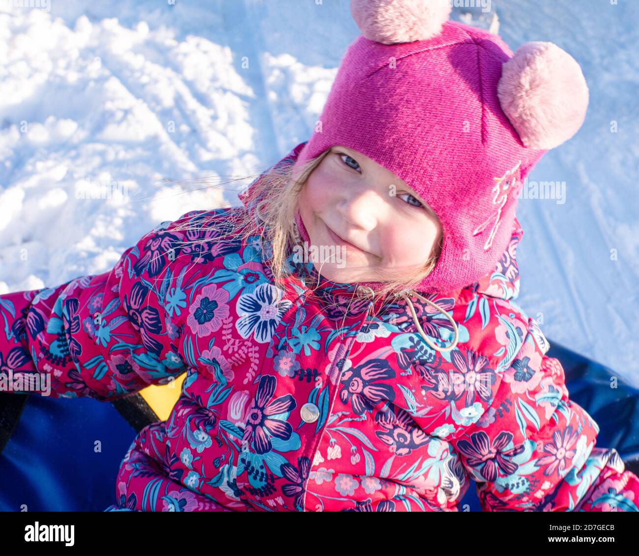Portrait of a smiling girl in a winter pink hat and jacket sits on a ...