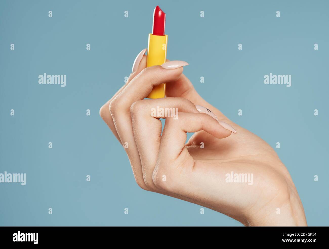 Woman holding lipstick in hand on blue background cropped view of model ...