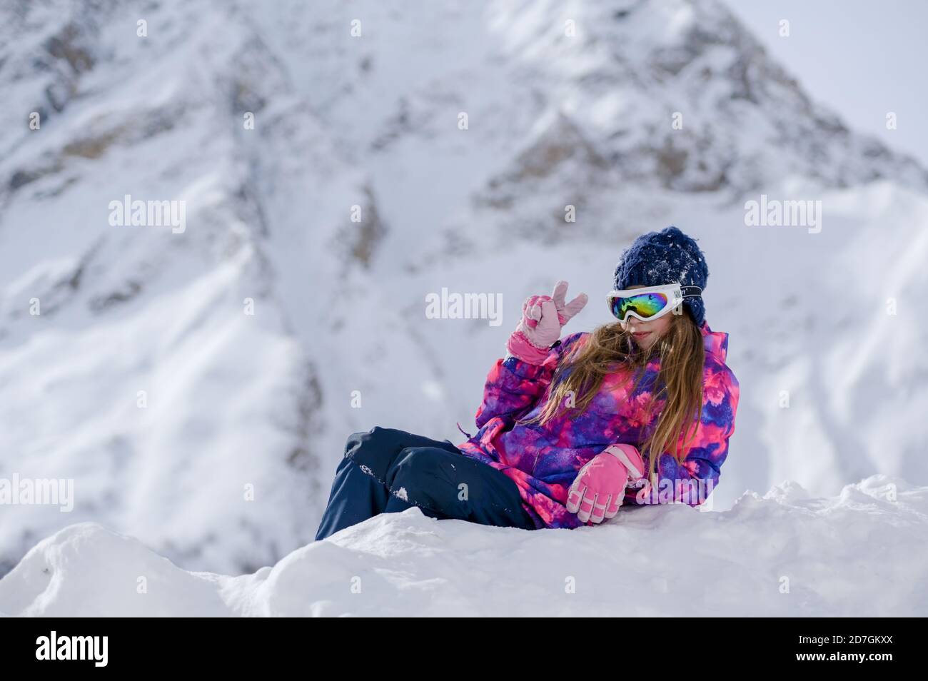 happy little girl in ski pink and violet suit lying on snow in alpine ...