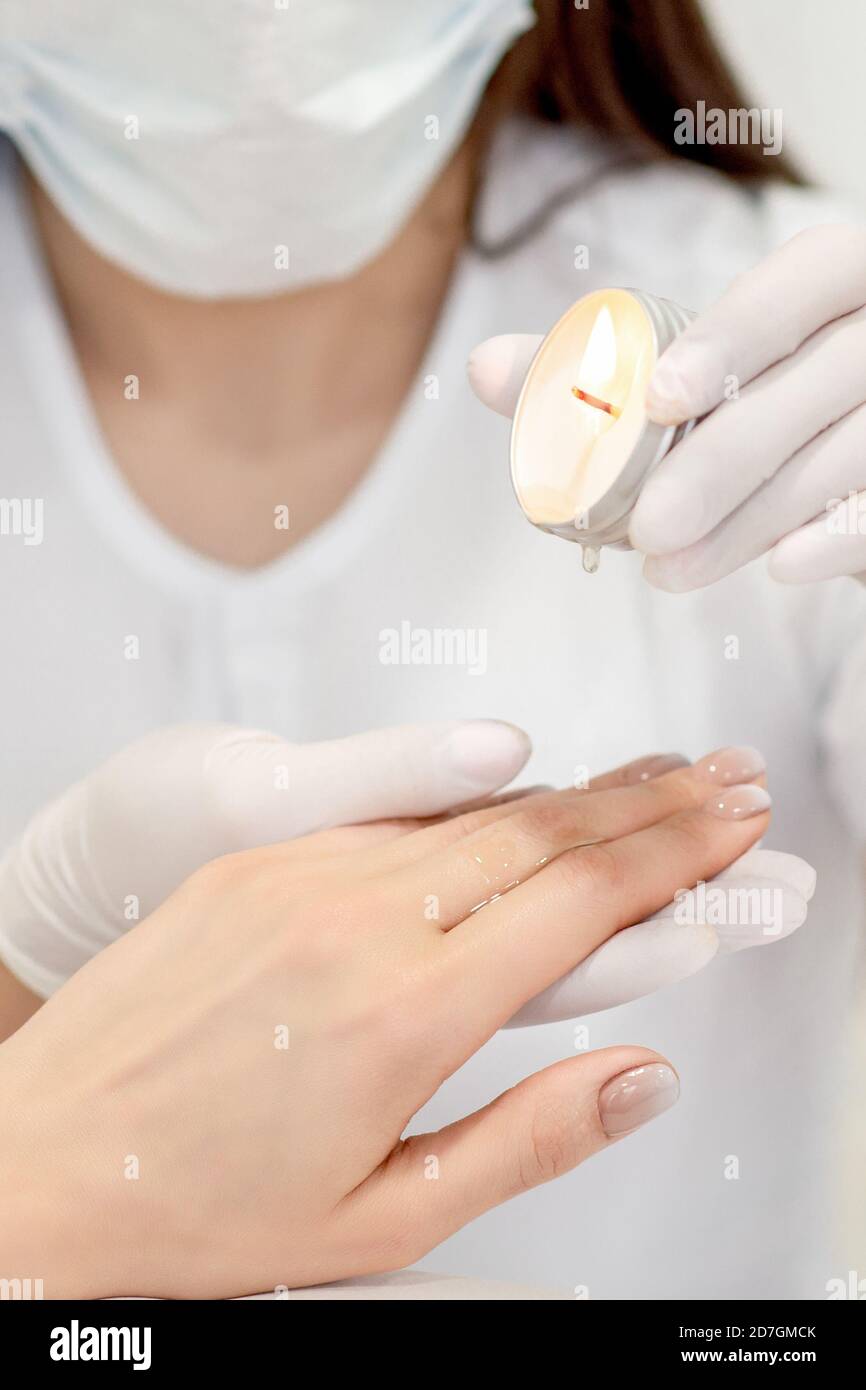 Manicure master applying warm wax from candle on fingernails of young ...