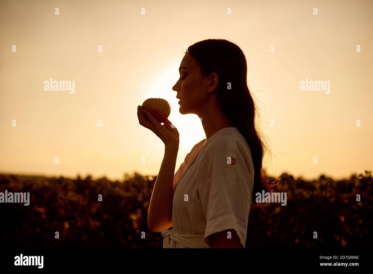 Girl with an apple posing in front of the camera in the sunset ...