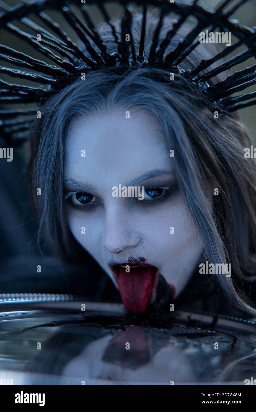 Portrait of young woman in image of vampire in black dress and crown on ...