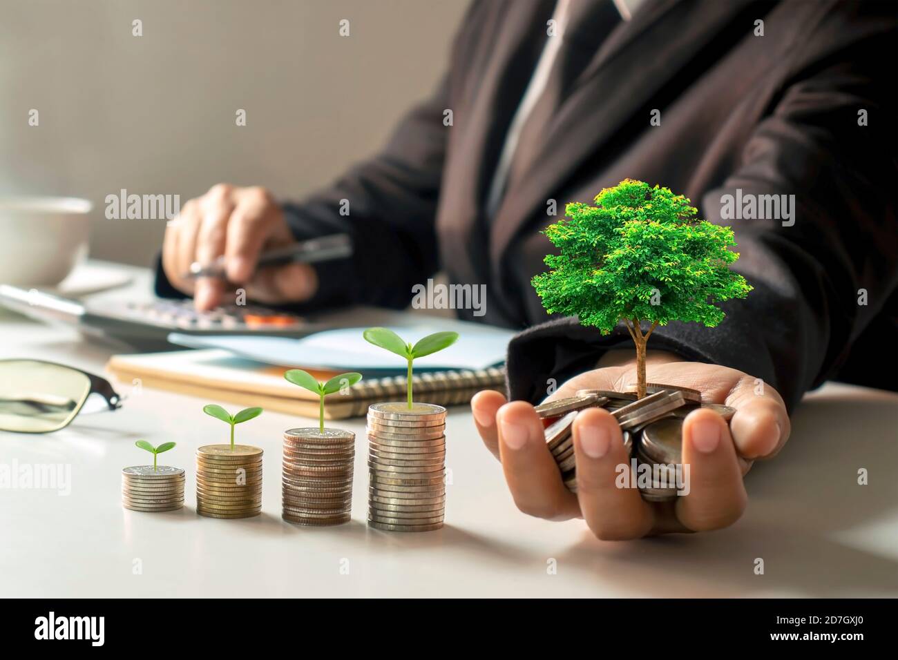 A growing tree on a pile of money in the hands of a businessman and a ...