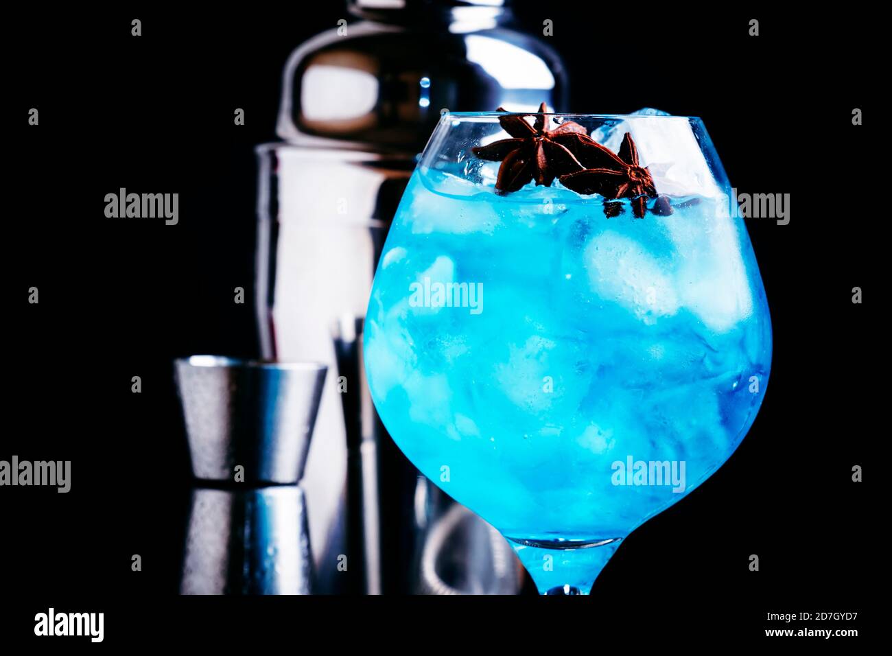 Blue cocktail with ice and anise in brandy glass, black background ...