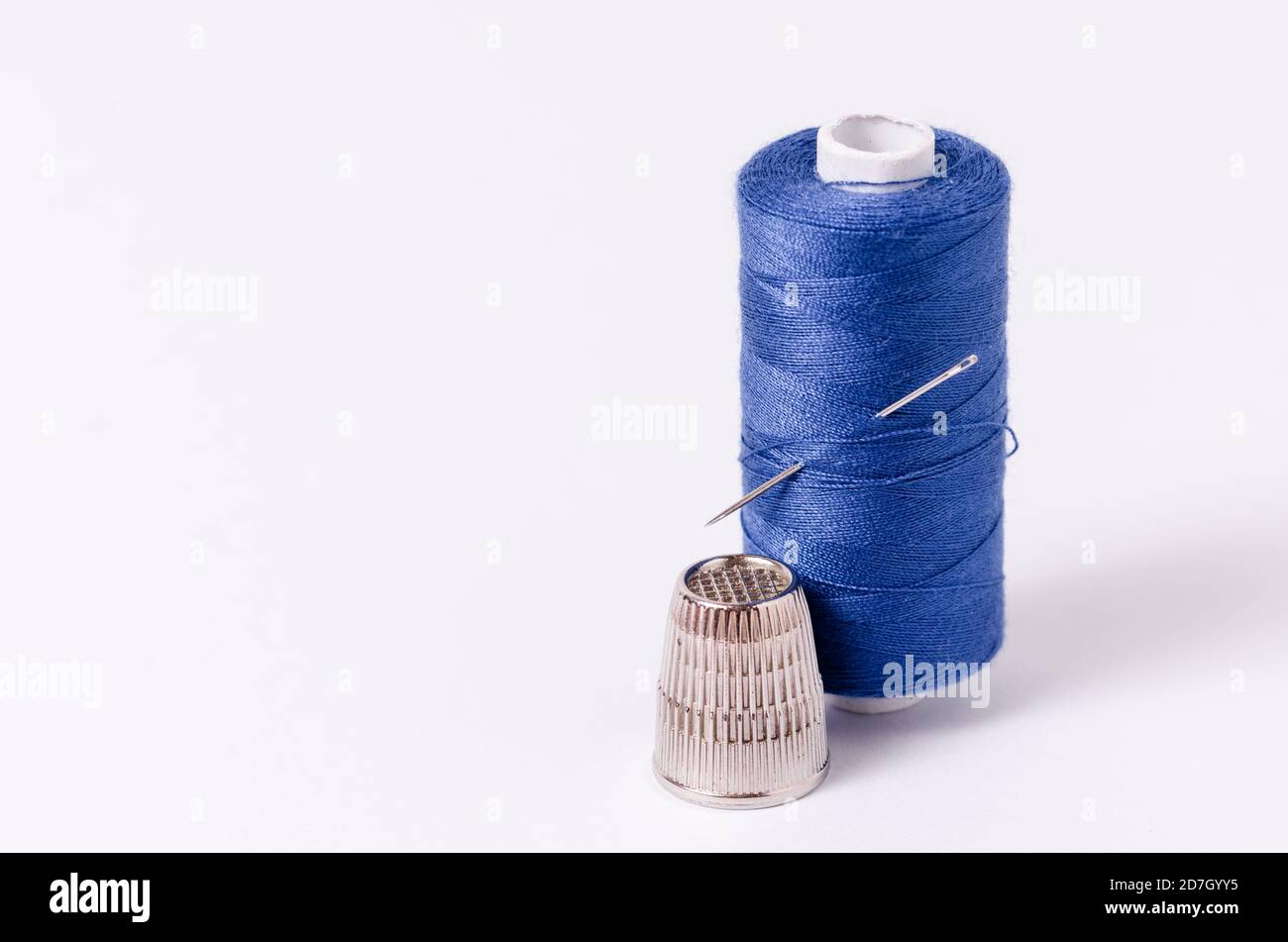 Spool of blue thread with needle and one metal thimble on white ...
