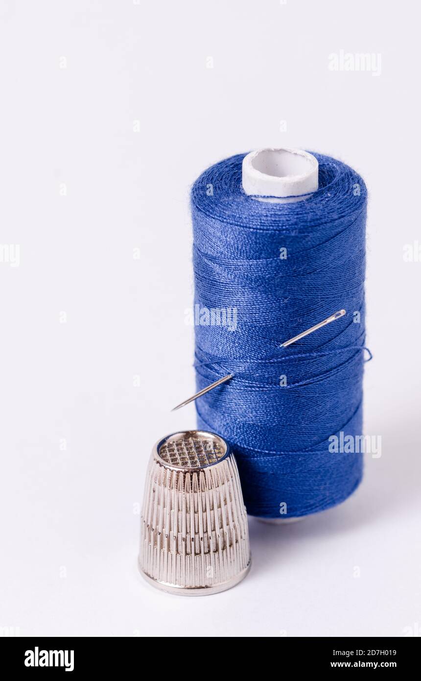 Spool of blue thread with needle and one metal thimble on white ...