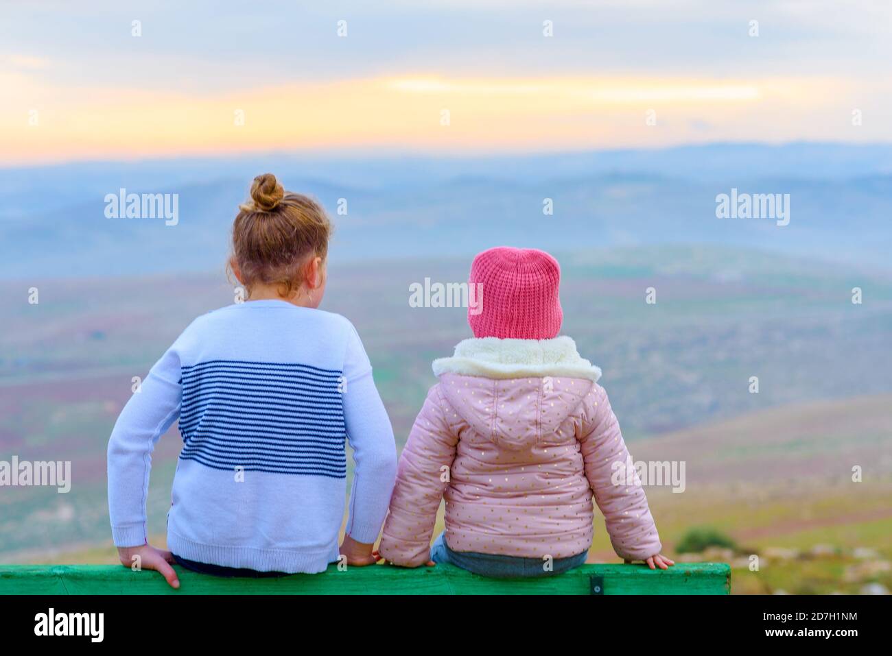 Happy little girls sitting on bench at beautiful landscape background ...