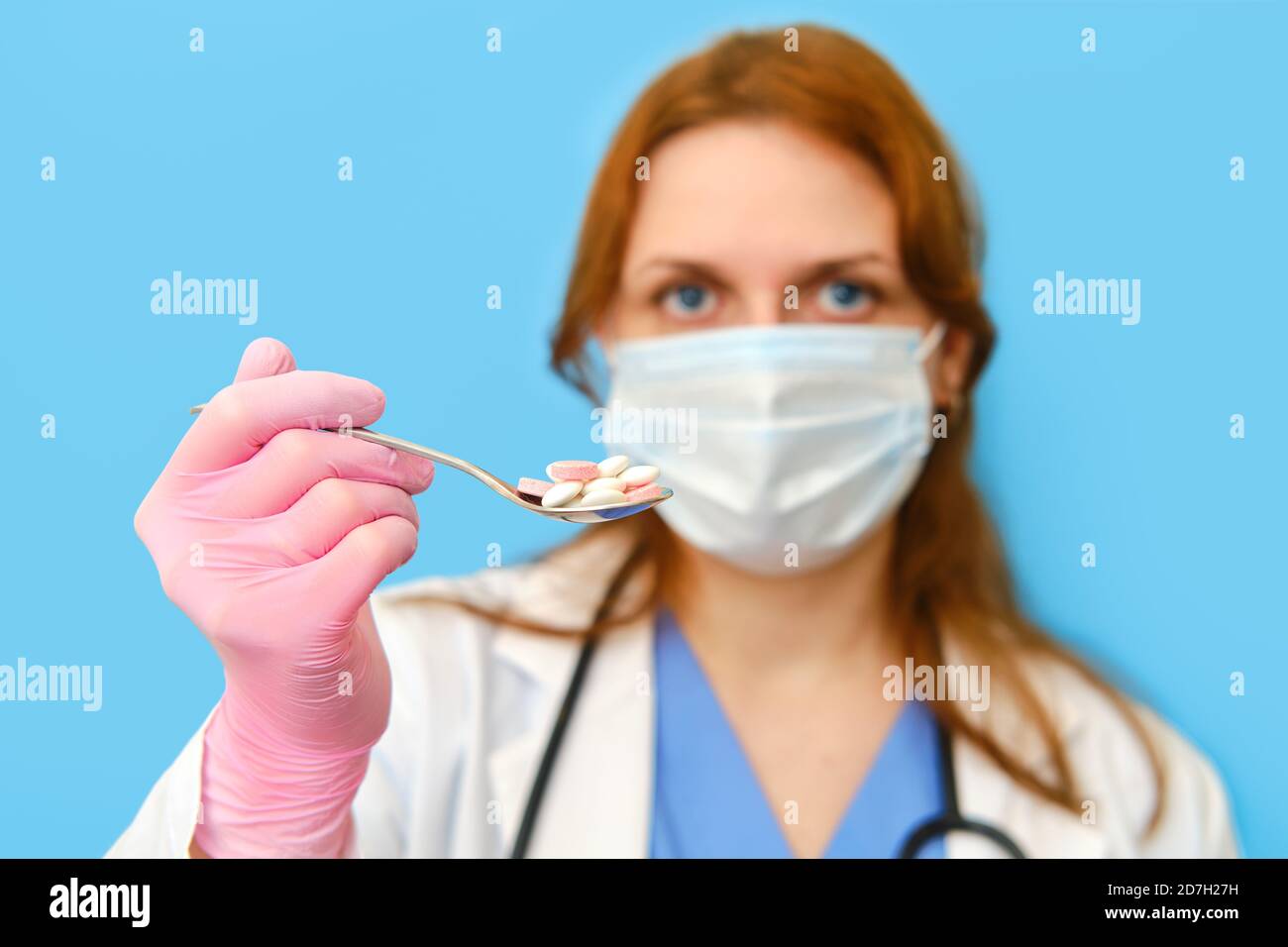Woman doctor holding a spoon with pills on a blue background, close-up ...