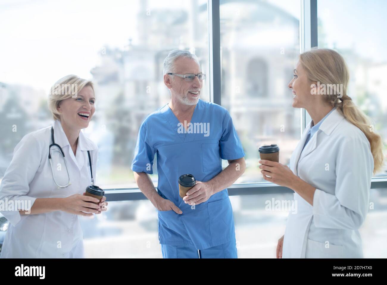 Group of smiling doctors drinking coffee next to the window, having ...