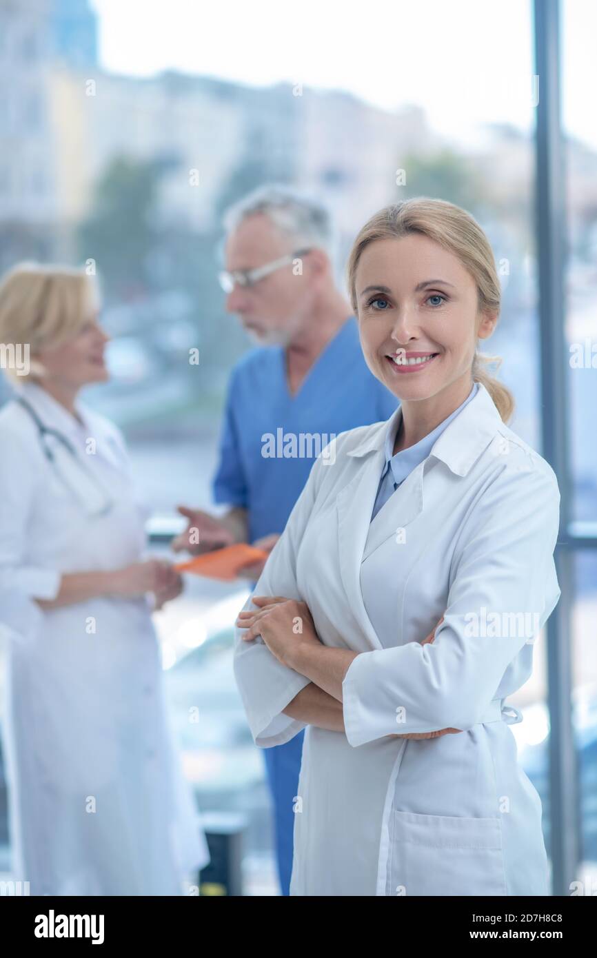 Female doctor looking with folded arms into camera, her colleagues ...