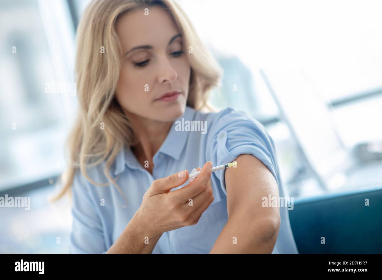 Blonde female making injection into her arm Stock Photo - Alamy
