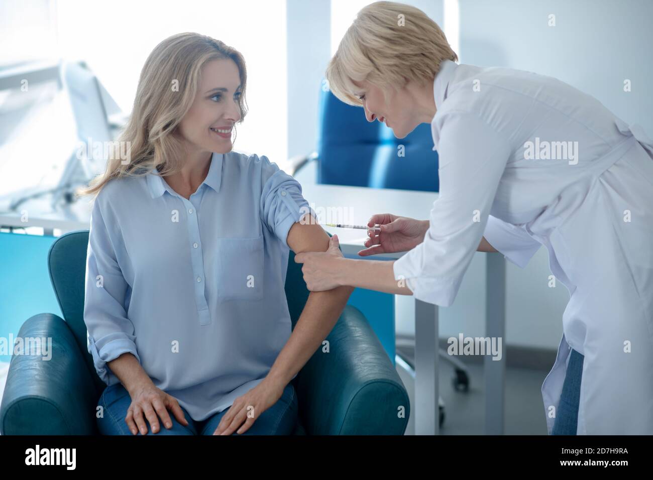 Blonde female doctor making injection into arm of smiling female ...