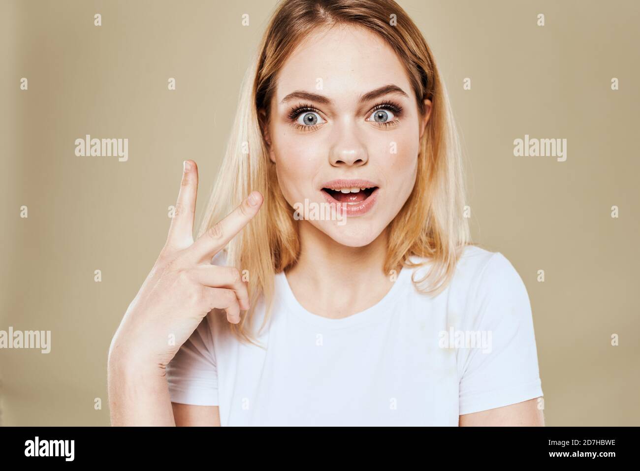 Cheerful blonde woman in a white T-shirt gestures with her hand emotions beige background Stock ...