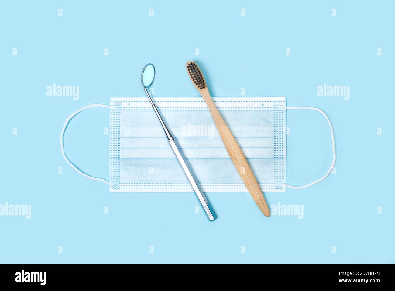 Dentist mirror and toothbrush on a surgery mask on a light blue ...