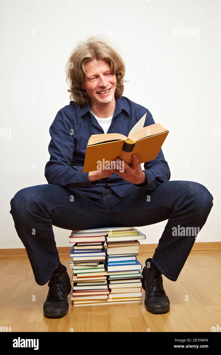 Man sitting on a pile of books and reading a book Stock Photo - Alamy