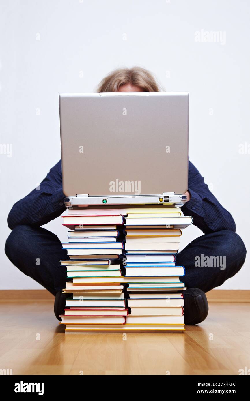 Man sitting behind laptop on pile of books Stock Photo - Alamy