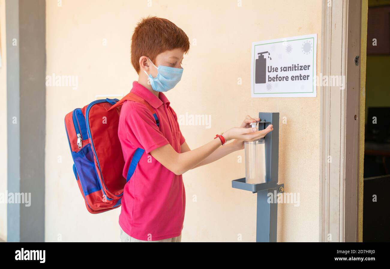 Kid with medical mask using hand sanitizer before entering classroom ...